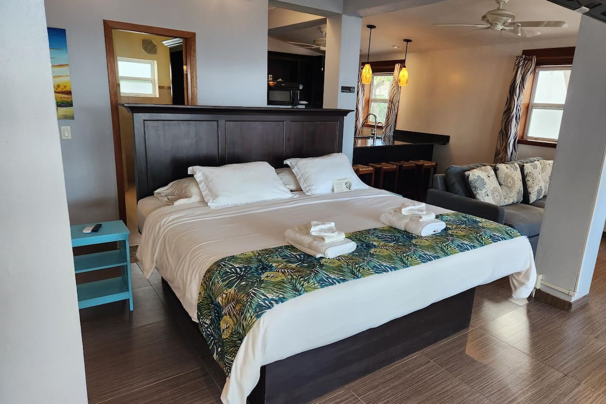 Quarto de hotel moderno com uma cama grande, um sofá, uma mesinha e um ventilador de teto.