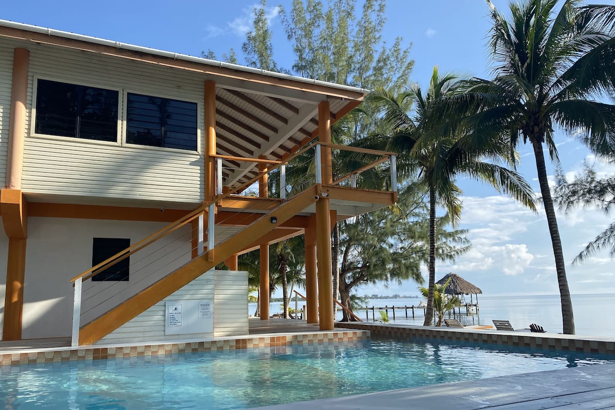 Uma área de piscina com deck de madeira, escadaria e vista para o oceano.