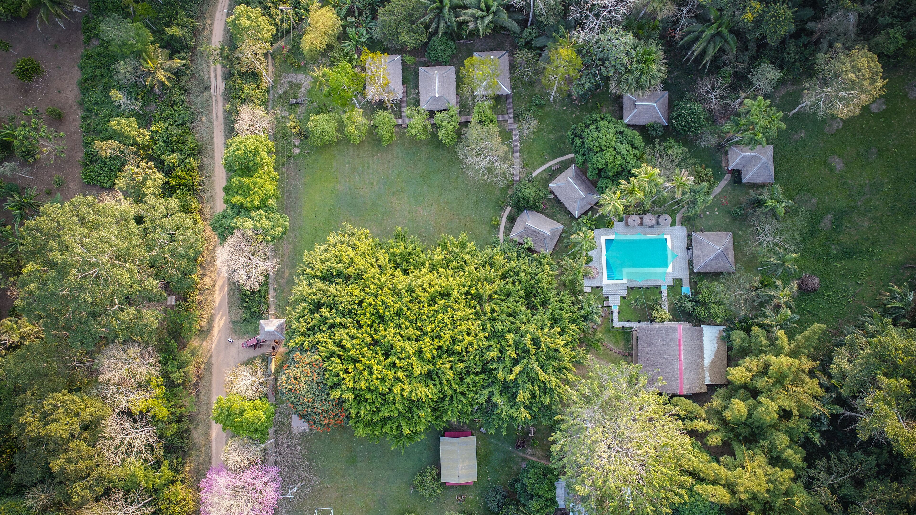 Vista aérea de um resort com várias acomodações em estilo bangalô, piscina central e vegetação exuberante ao redor da propriedade.