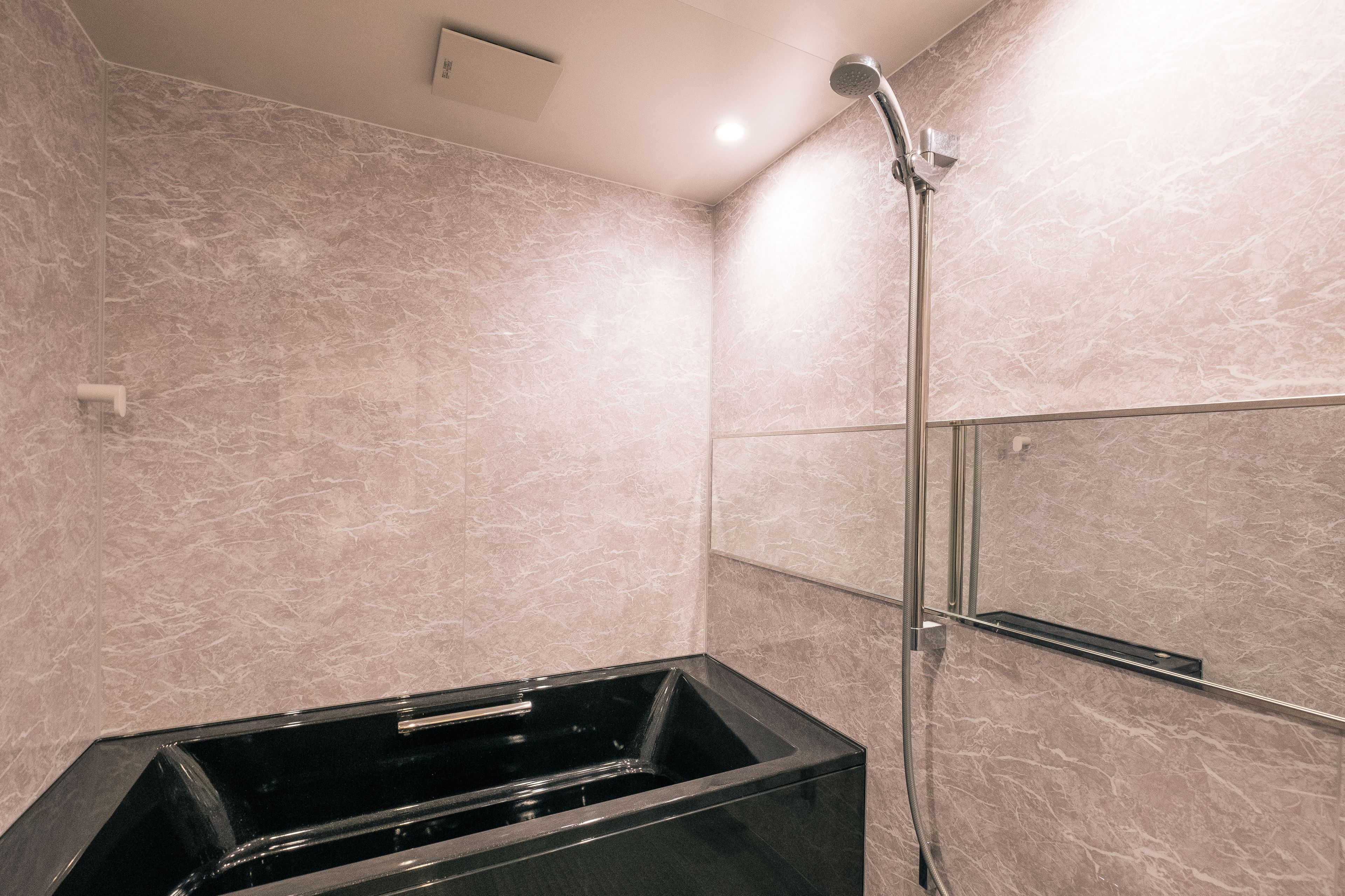Uma casa de banho moderna com banheira de hidromassagem protegida por vidro, chuveiro com chuveiro manual e paredes de mármore.