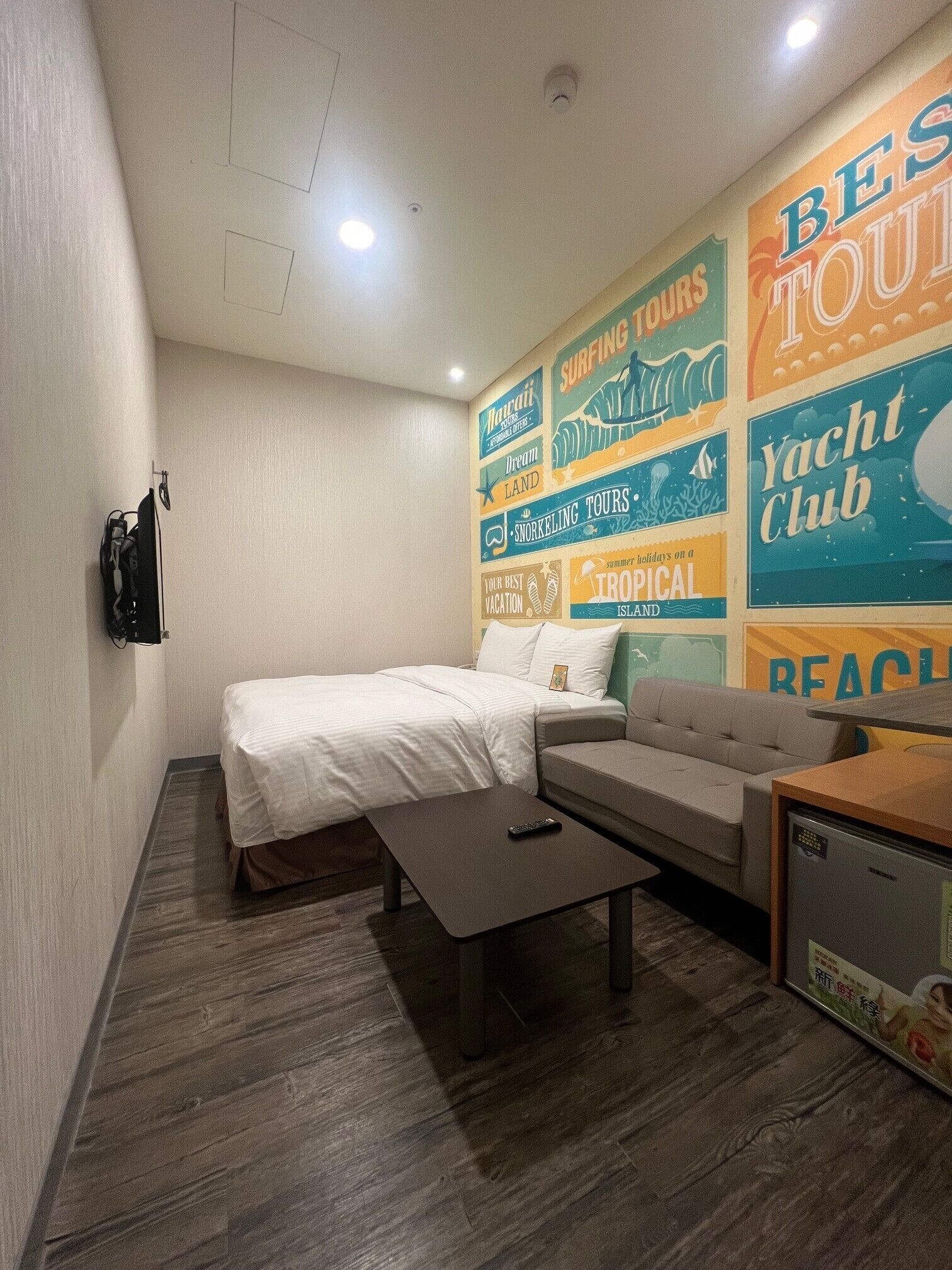 Quarto de hotel com cama, sofá, mesa pequena e parede decorada com cartazes de viagens.