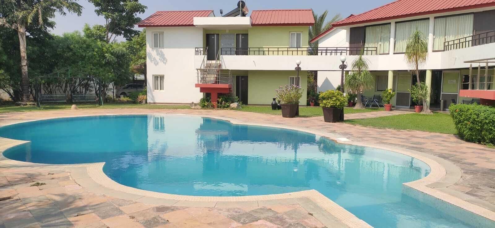 Um hotel com piscina, um edifício de dois andares e um jardim bem cuidado.