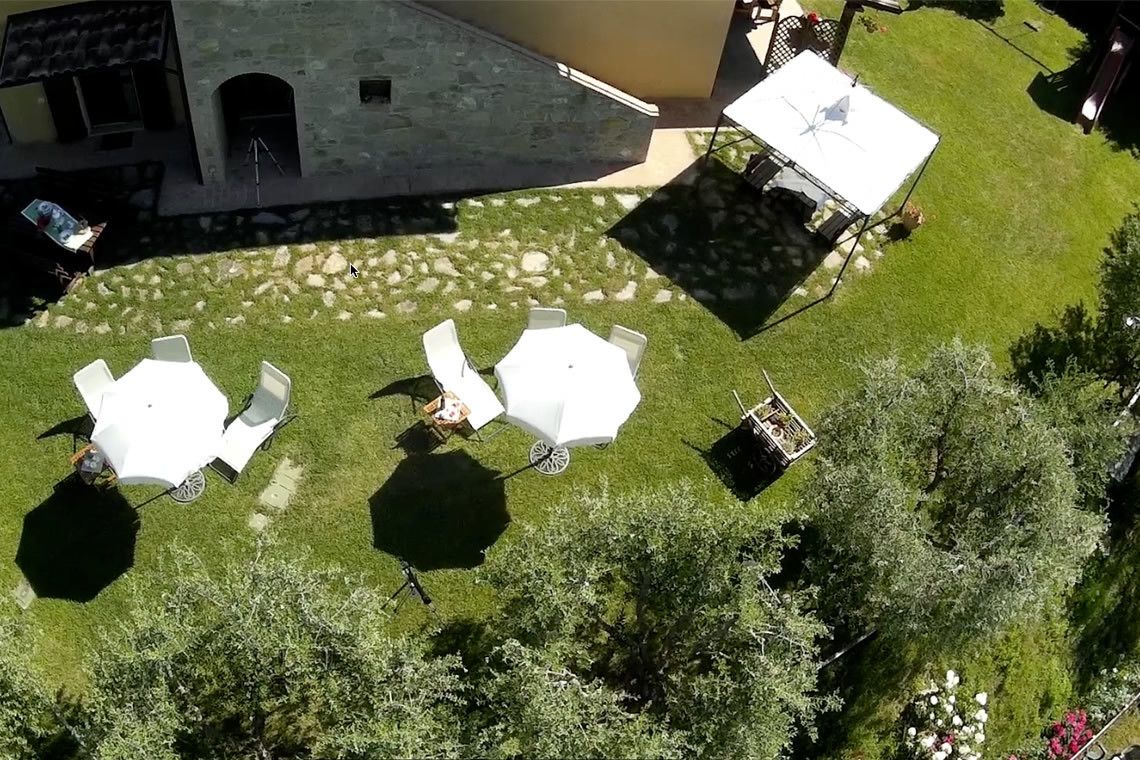 Um pátio ao ar livre com mesas e cadeiras brancas, rodeado por vegetação e um edifício de pedra.