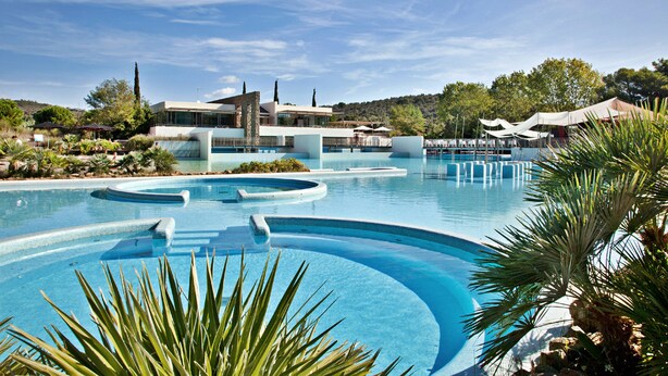 Um resort moderno com uma ampla piscina infinita, bar na piscina e montanhas ao fundo.