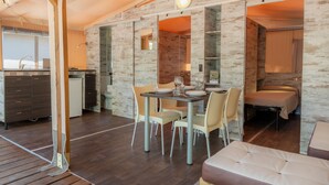 Uma sala de jantar com uma mesa posta para quatro pessoas, piso de madeira e teto coberto.