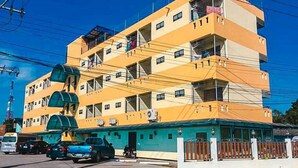 Um edifício com vários andares, varandas, portão fechado e veículos estacionados na frente.