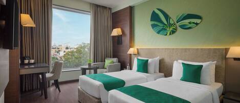 Quarto de hotel com duas camas, uma escrivaninha, uma cadeira, uma televisão e uma janela com vista para prédios.