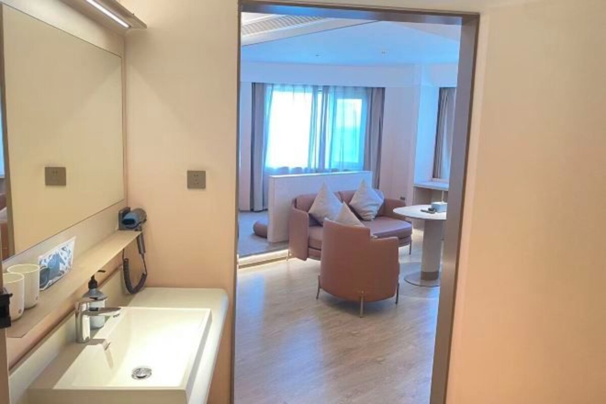 Quarto de hotel com banheiro, área de estar com sofá e uma mesinha, e vista para o exterior.