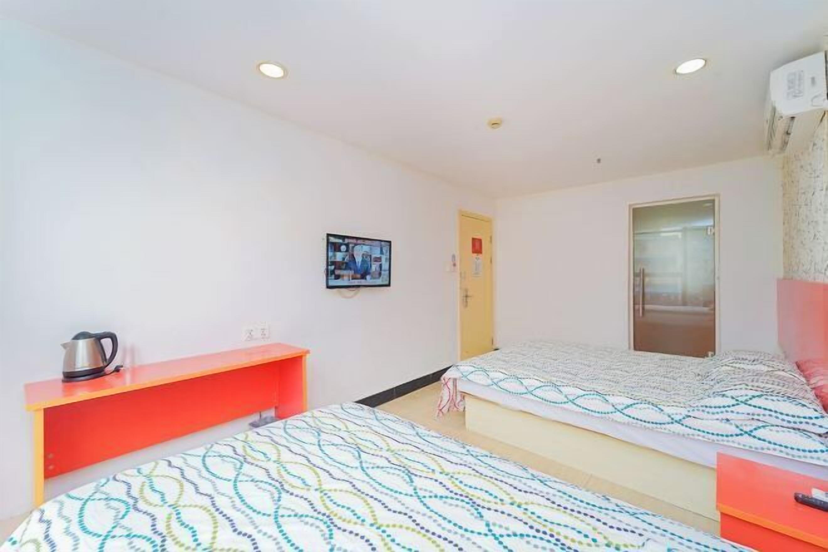 Quarto com duas camas, uma escrivaninha vermelha, chaleira e um quadro na parede.