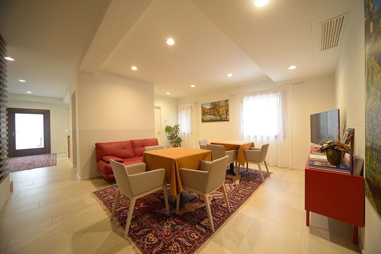 Uma sala de estar moderna com um sofá vermelho, uma mesa de jantar de madeira com cadeiras, uma mesinha lateral vermelha com uma planta, e uma TV em um suporte.