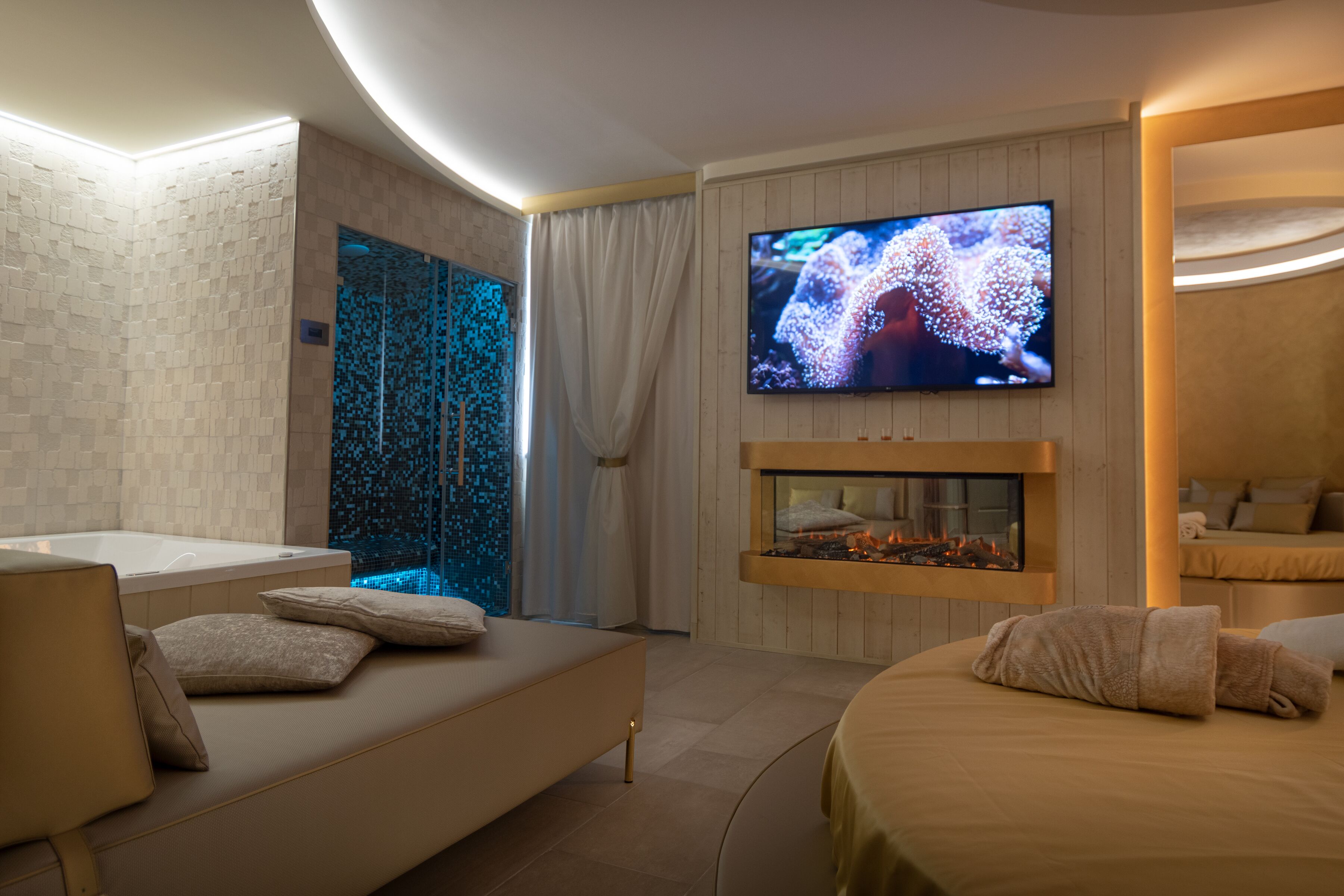 Quarto de hotel moderno com uma televisão de tela plana grande, lareira, banheira e uma área de estar aconchegante.