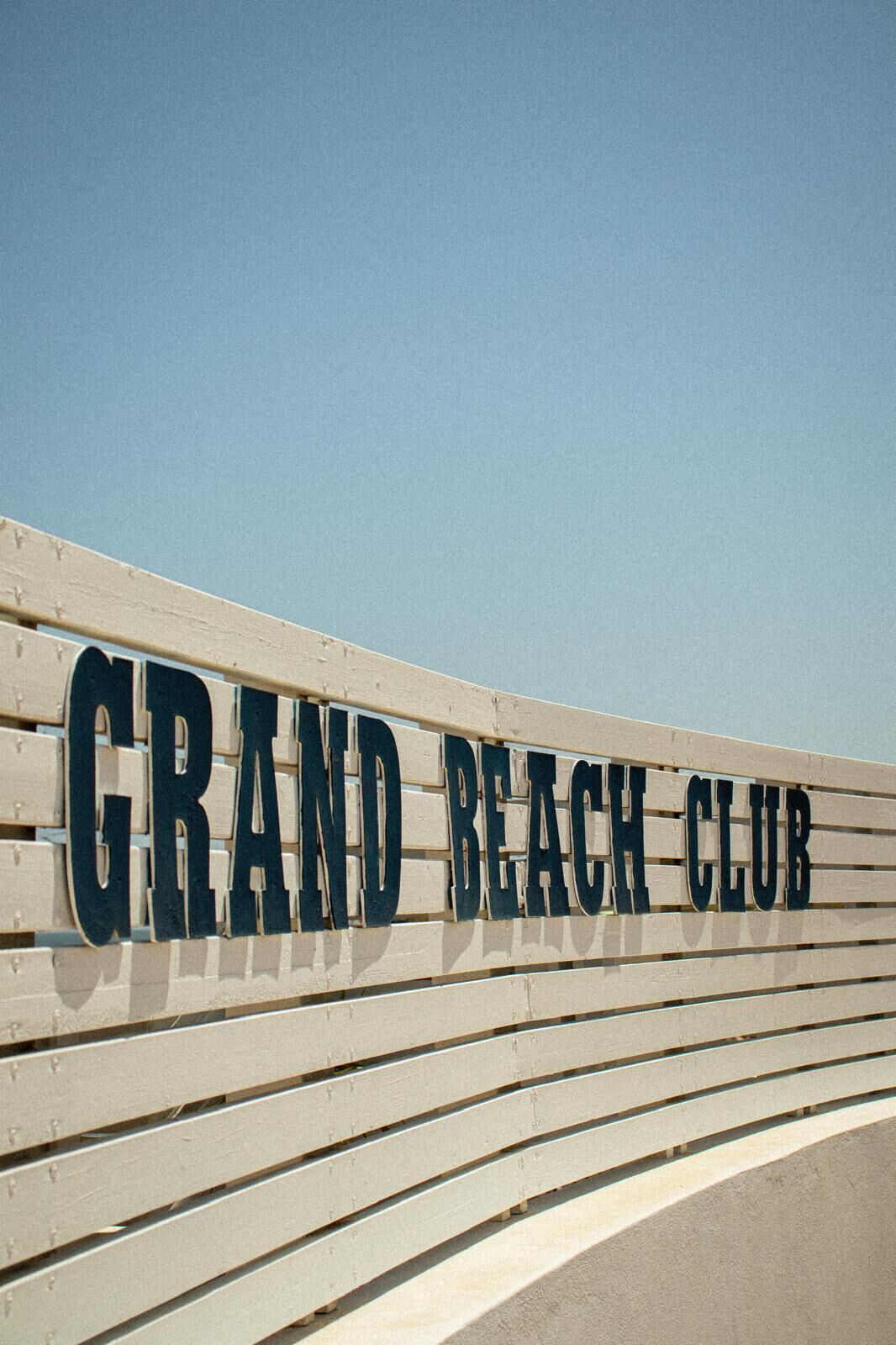 Uma placa de madeira com a inscrição 'GRAND BEACH CLUB' em letras maiúsculas.
