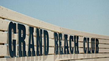 Uma placa de madeira com a inscrição 'GRAND BEACH CLUB' em letras maiúsculas.