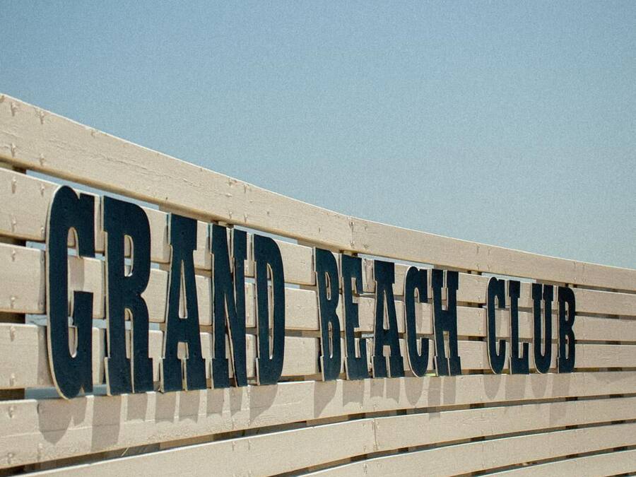 Uma placa de madeira com a inscrição 'GRAND BEACH CLUB' em letras maiúsculas.