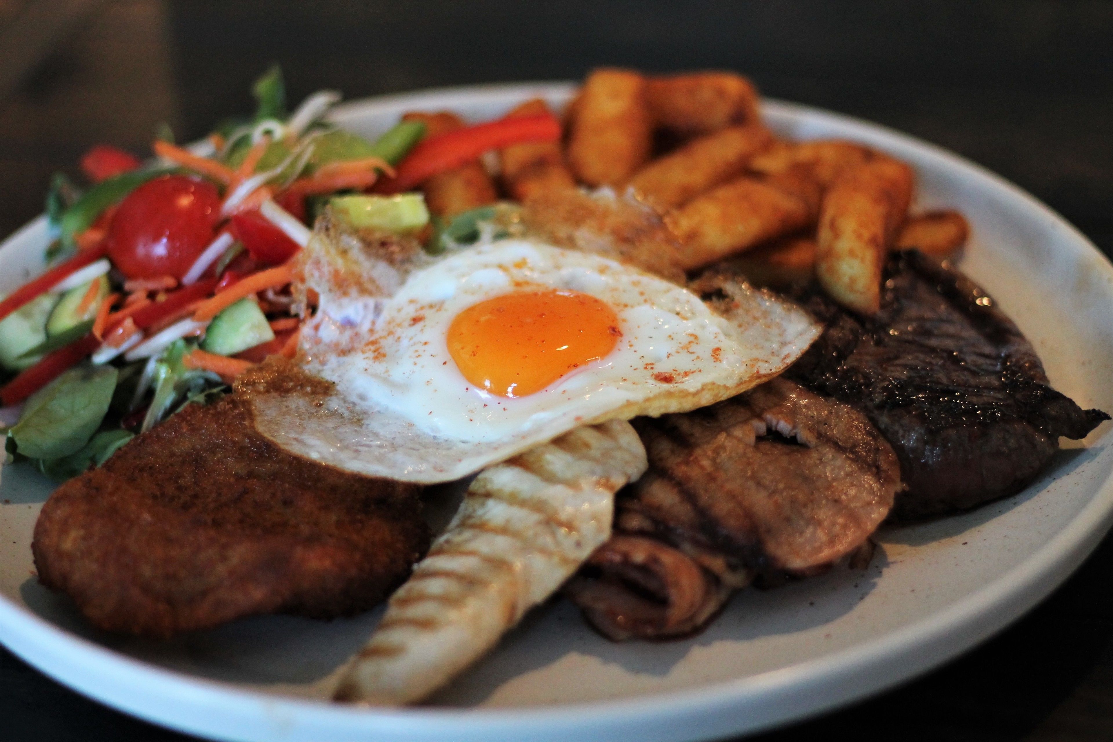 Prato de comida com ovo frito, bife e legumes.