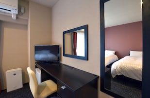 Quarto de hotel com uma cama, uma escrivaninha com cadeira, televisão e espelho.