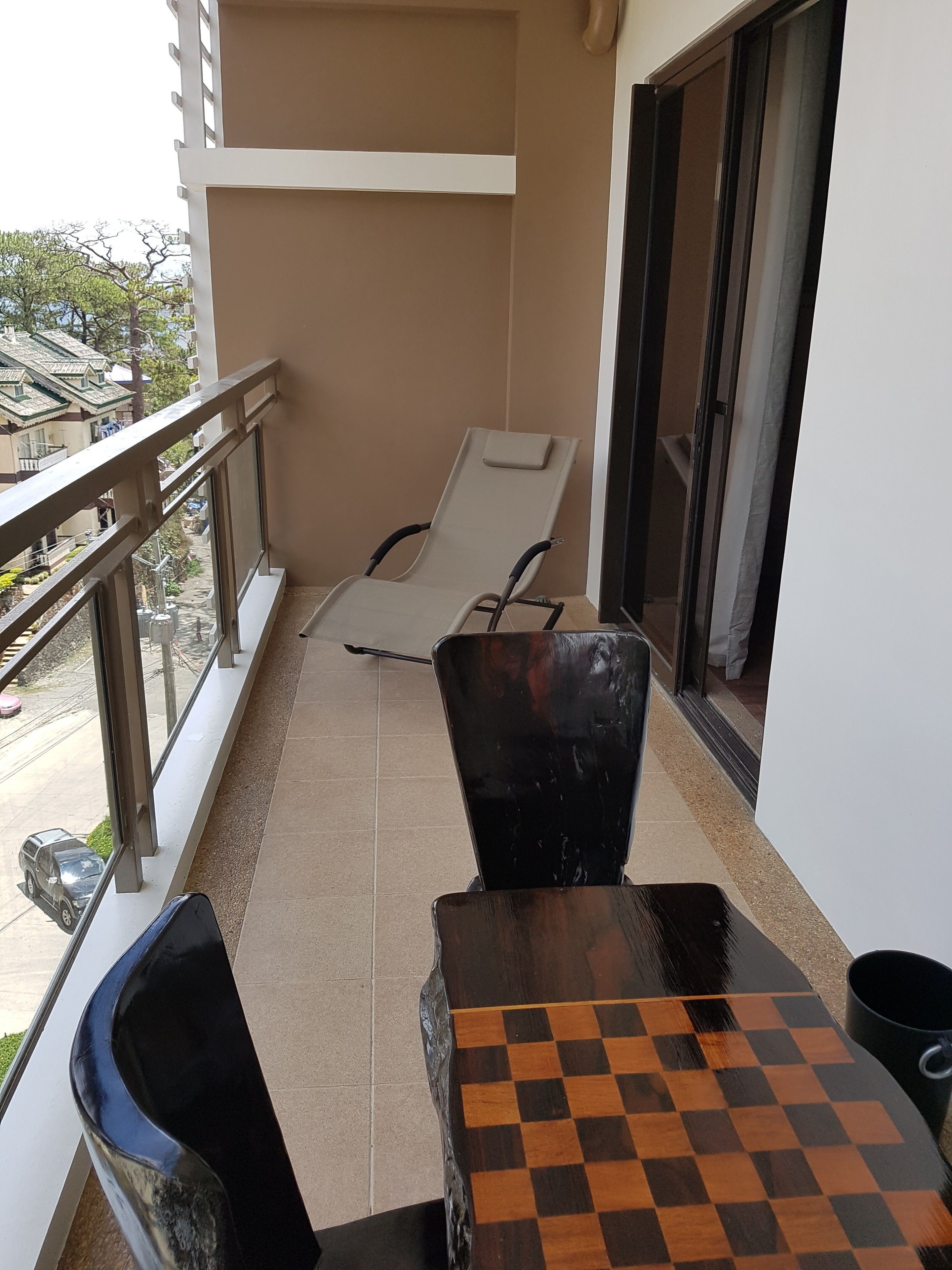 Uma varanda com mesa e cadeiras, vista para a rua e um prédio ao fundo.