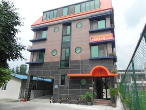Um hotel de vários andares com design moderno, com um toldo laranja chamativo e uma placa indicando que é uma pensão e hotel.