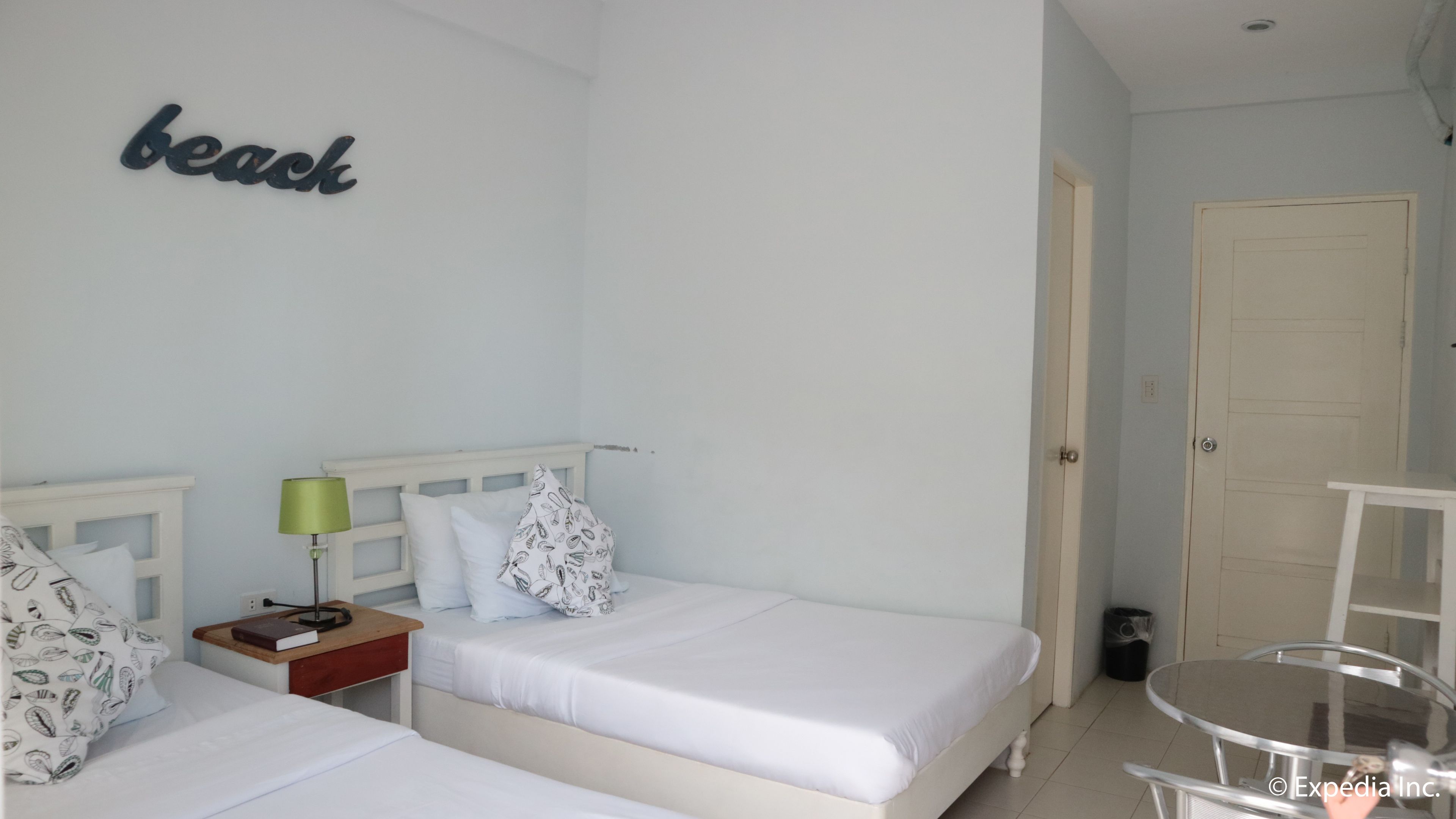 Quarto de hotel com duas camas, uma mesa de cabeceira com abajur, uma mesinha e uma cadeira.