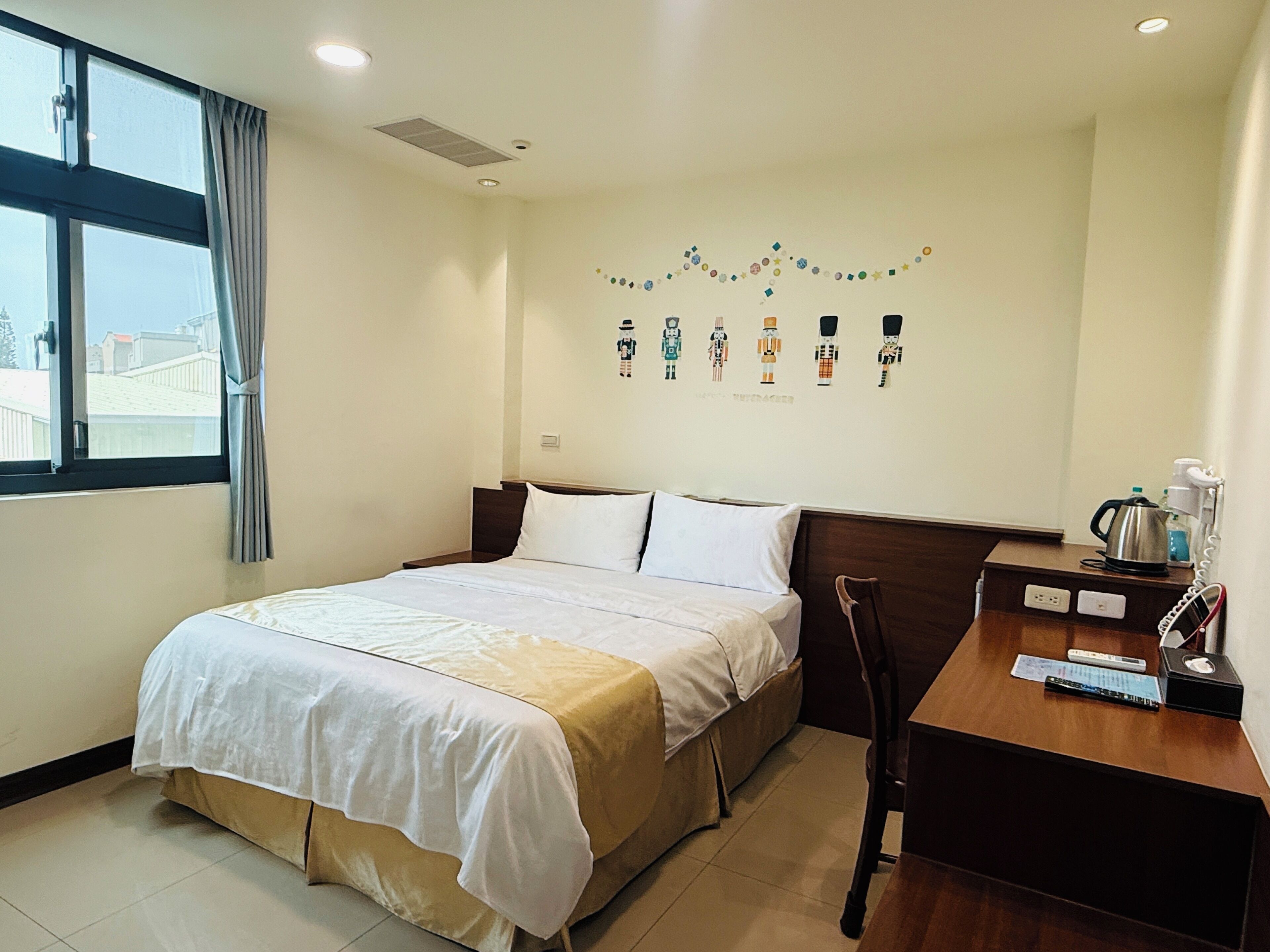 Quarto de hotel com cama, escrivaninha de madeira, cadeira e um objeto decorativo na parede.