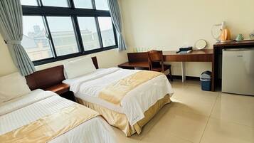 Quarto de hotel com duas camas, uma escrivaninha, uma cadeira, um mini frigorífico e uma janela com cortinas.