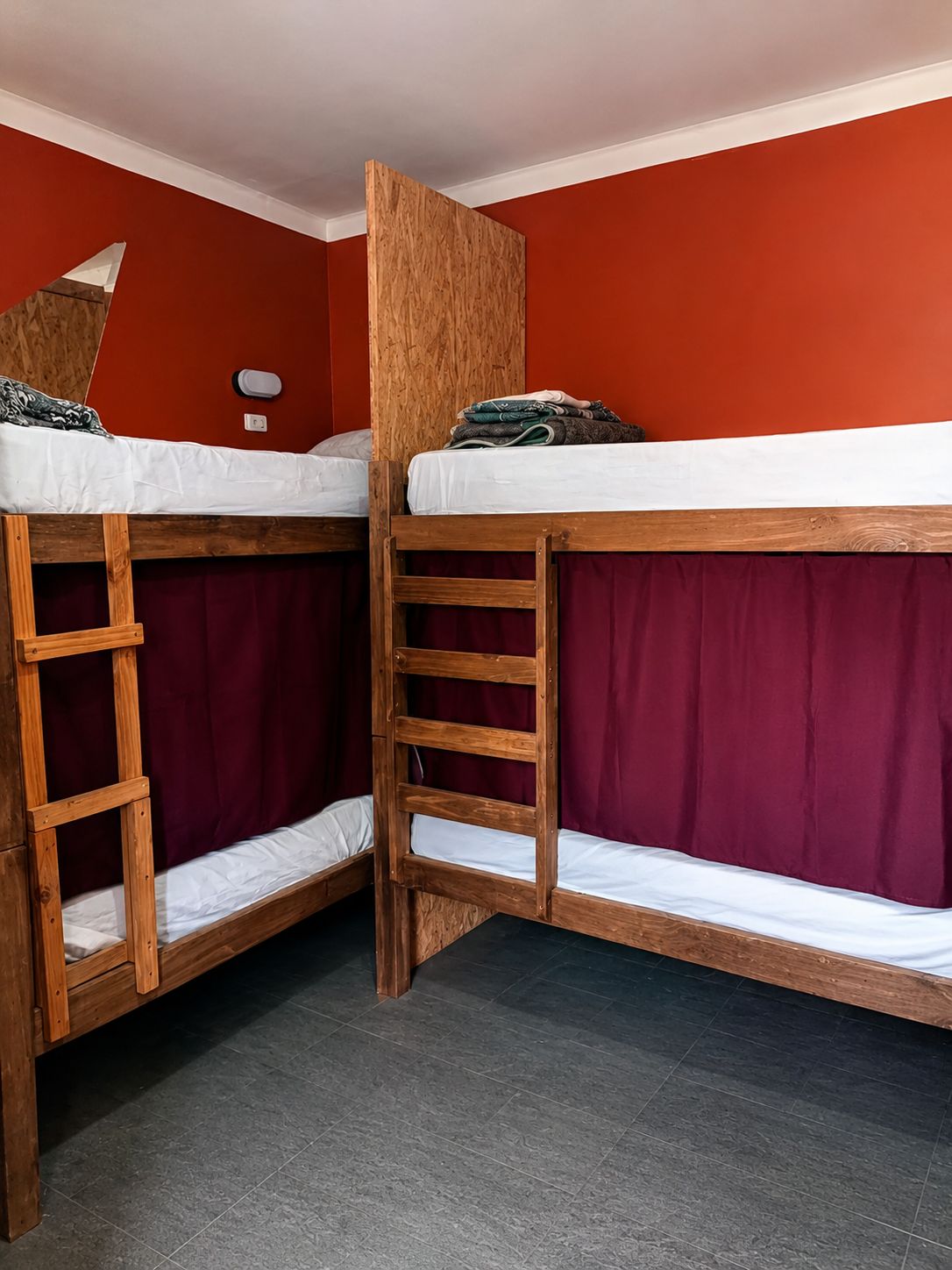 Quarto com beliches de madeira, escada e parede vermelha.