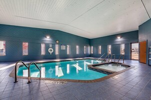 Piscina interior com área de mergulho, piso ladrilhado e um relógio na parede.