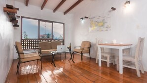 Um quarto com piso de madeira, um sofá, uma mesa de jantar com cadeiras, um laptop e uma garrafa de vinho.