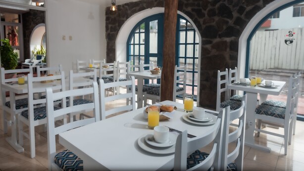 Uma sala de jantar com mesas e cadeiras brancas, paredes de pedra e janelas em arco.