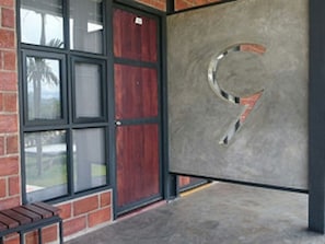 Entrada de edifício com um grande letreiro de metal com o número 7, paredes de tijolo e um banco do lado de fora.