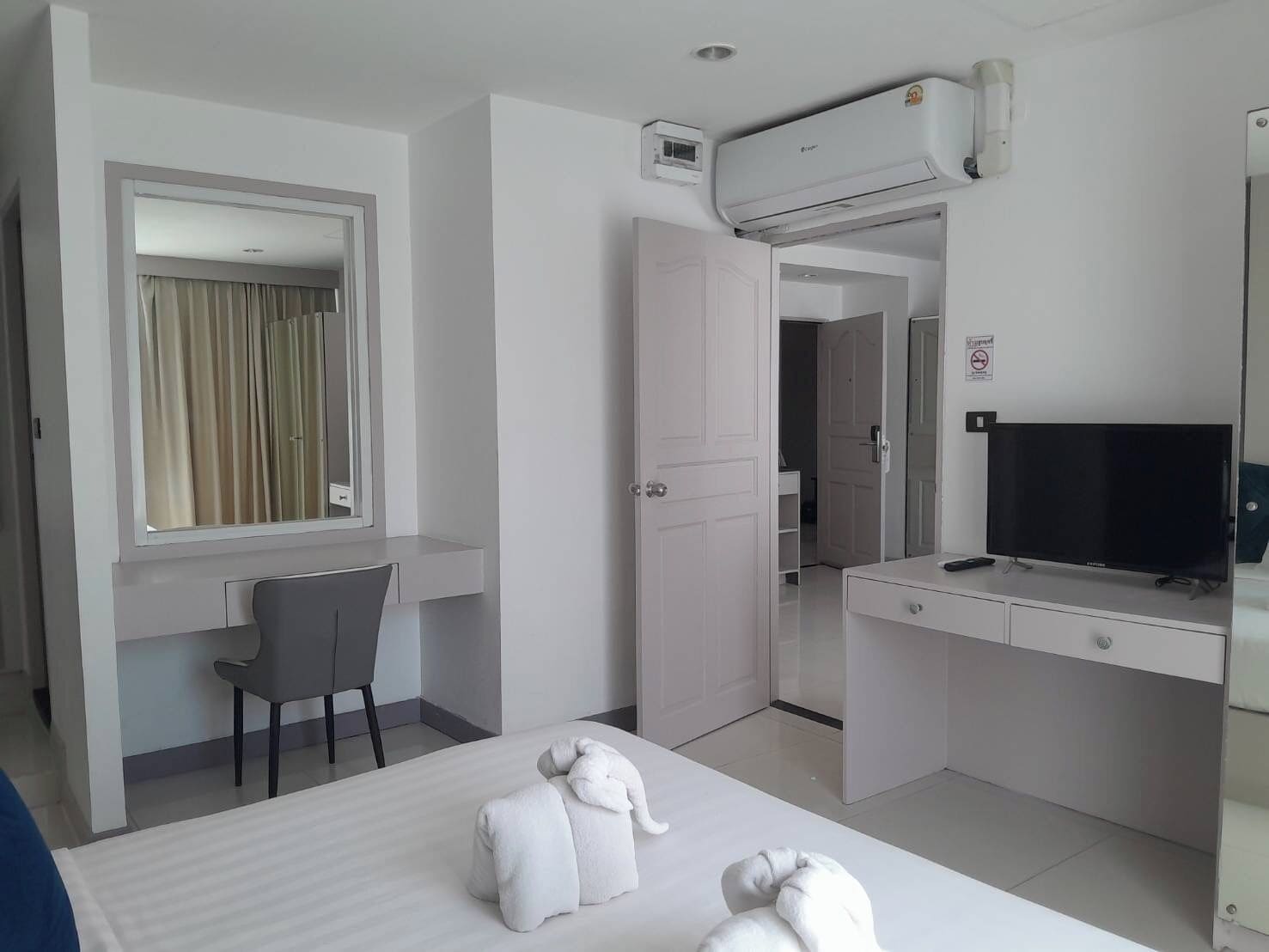 Quarto de hotel com cama, escrivaninha, cadeira, ar condicionado, televisão e guarda-roupa.