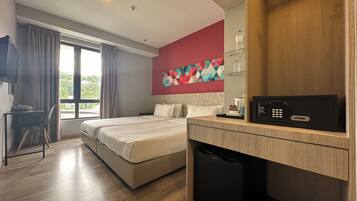 Quarto de hotel com cama, escrivaninha, micro-ondas e janela com cortinas.