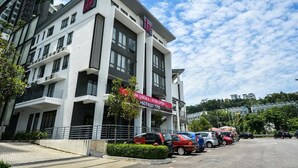 Um hotel moderno com fachada branca, várias varandas e um estacionamento com diversos carros.