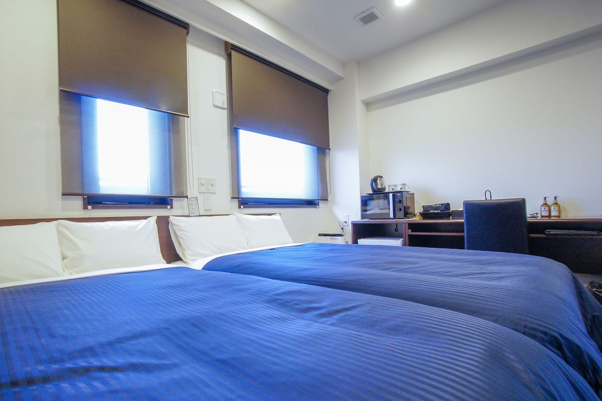 Quarto de hotel com duas camas, uma escrivaninha, uma cadeira, micro-ondas e minibar.