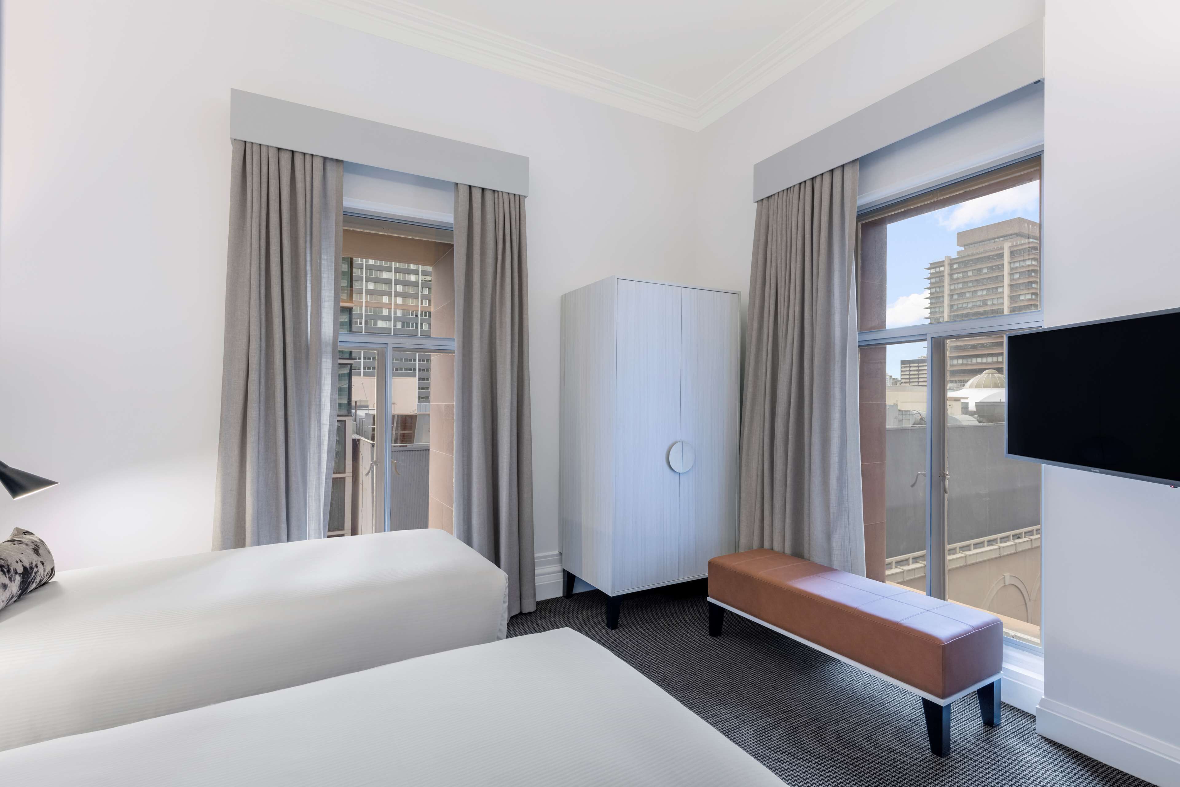 Quarto de hotel com duas camas, um banco, um guarda-roupa e uma televisão.