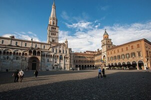 Uma praça histórica com uma igreja de destaque, apresentando uma alta torre de sinos e uma torre menor adjacente.