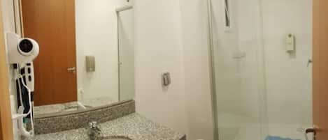 Casa de banho com lavatório em bancada de granito, espelho, sanita e cabine de duche em vidro.