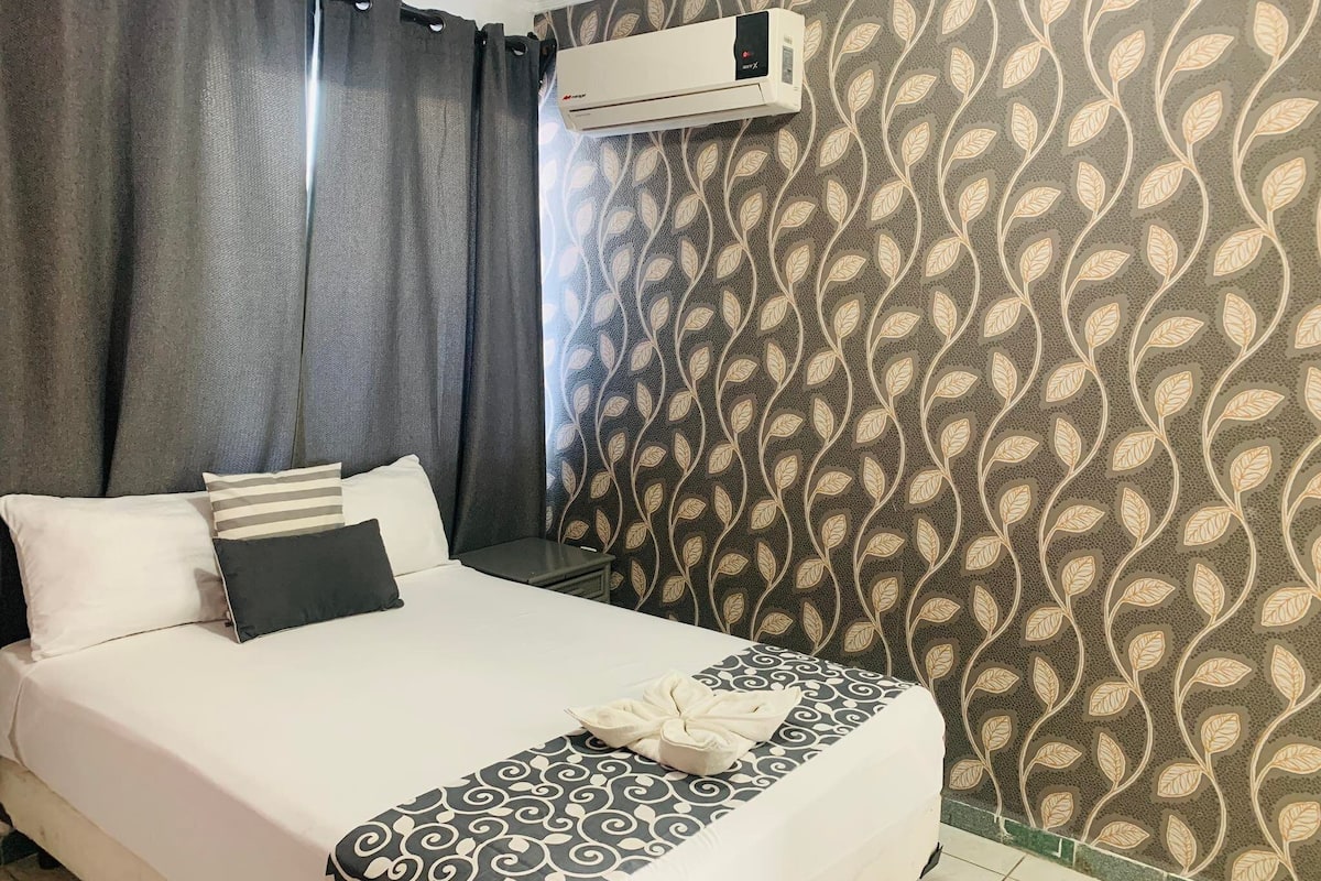 Quarto de hotel com cama, cortinas, ar condicionado e parede estampada.