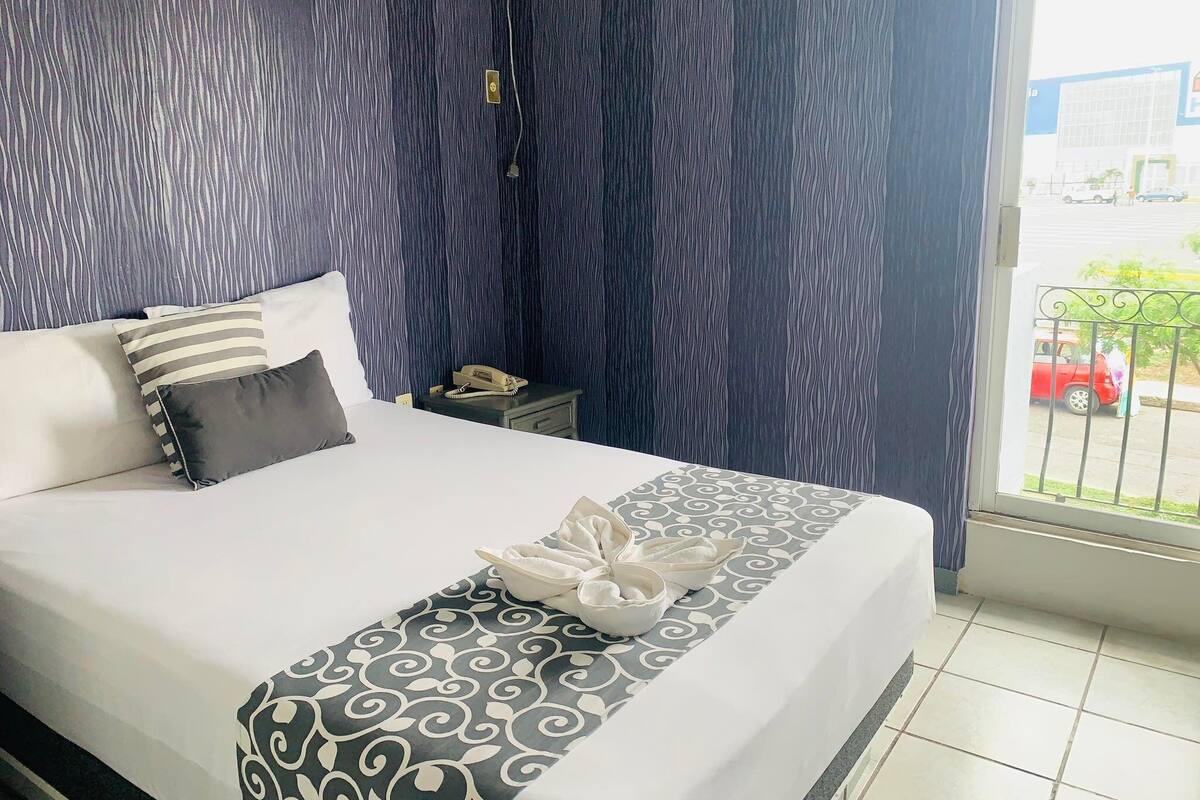 Quarto de hotel com cama, mesa de cabeceira, telefone e vista para o exterior.