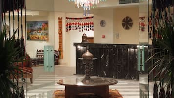 Uma área de recepção com um candelabro, um balcão de atendimento, um relógio de parede e um painel decorativo.