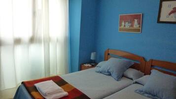 Quarto de hotel com duas camas, uma parede azul e uma janela com cortinas brancas.