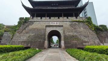 Um portão chinês tradicional com telhado ladrilhado e um arco, rodeado por vegetação.