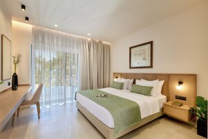 Quarto de hotel moderno com uma cama grande, uma escrivaninha e uma cadeira. Há uma janela com cortinas leves e uma moldura com uma imagem na parede.