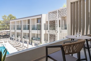 Varanda de hotel com cadeiras de lounge, piscina e vista do interior do edifício.