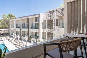 Varanda de hotel com cadeiras de lounge, piscina e vista do interior do edifício.