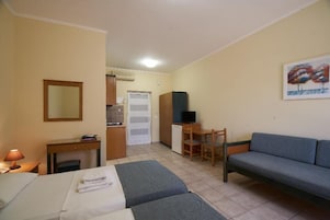 Quarto com cama, escrivaninha, poltrona, sofá, televisão e um quadro na parede.