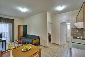 Um espaço de estar compacto com cozinha compacta, área de refeições com mesa e cadeiras, sofá e janela com cortinas.
