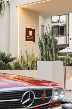 Um edifício moderno com uma placa indicando 'INEA SOLE BOUTIQUE HOTEL' e um carro vermelho ao primeiro plano.