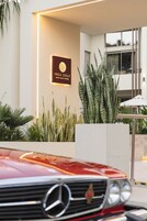 Um edifício moderno com uma placa indicando 'INEA SOLE BOUTIQUE HOTEL' e um carro vermelho ao primeiro plano.