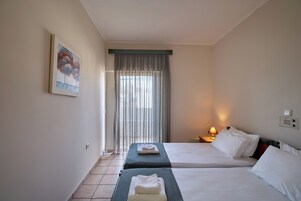 Quarto de hotel com duas camas, um quadro na parede, uma janela com cortinas leves e um abajur.